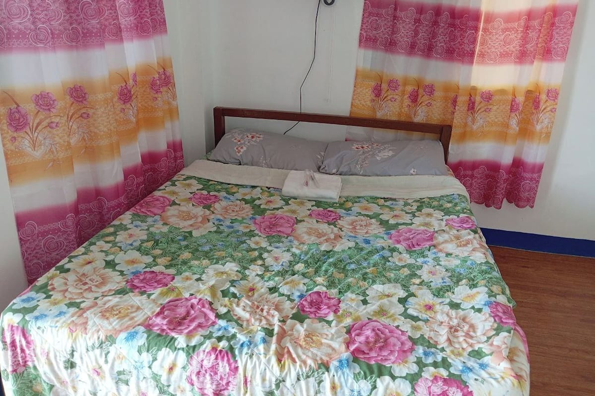 Uma cama com colcha florida, cortinas com padrão de corações e cabeceira de madeira.