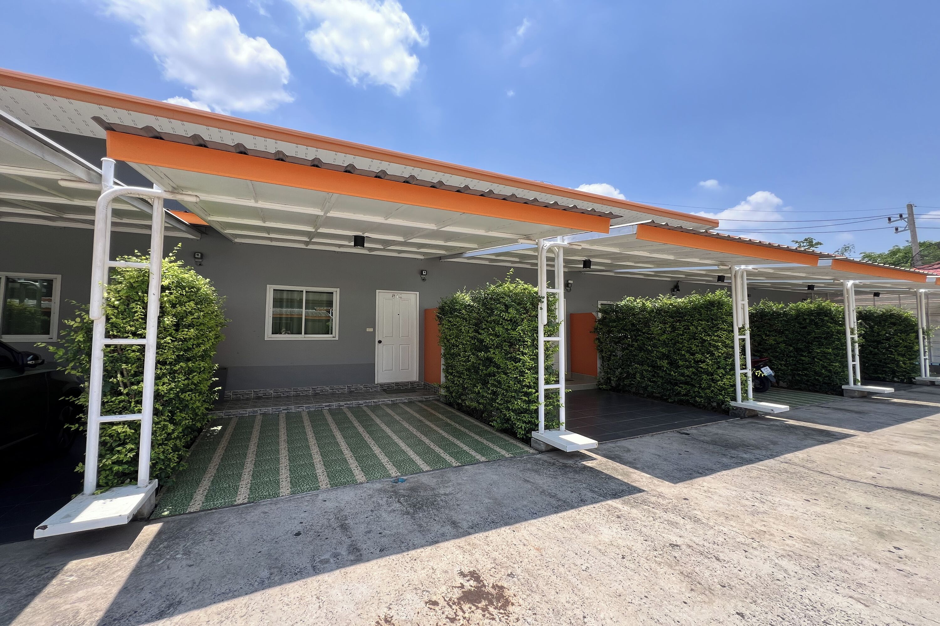 Área de estacionamento coberta com garagem, porta e pequeno jardim com tapete verde e arbustos.
