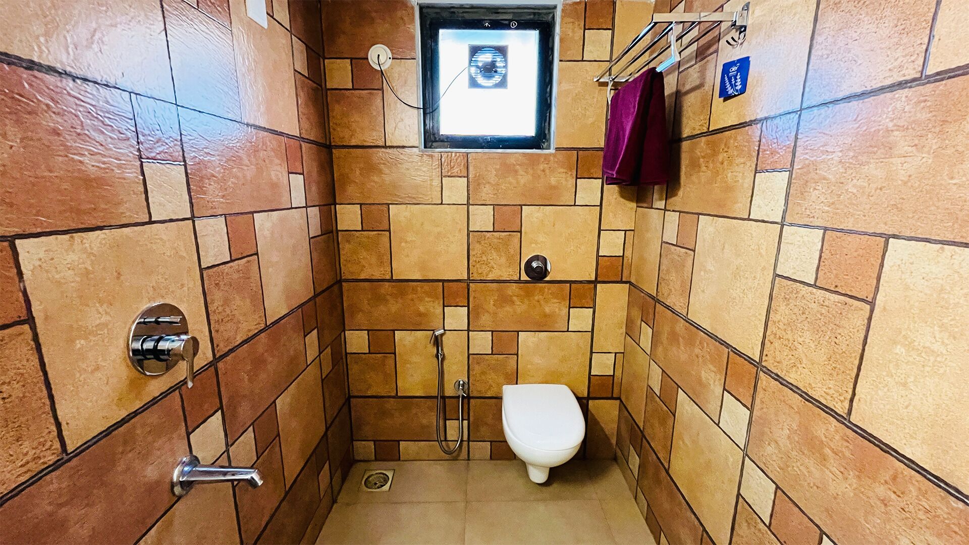 Casa de banho pequena, com azulejos, sanita, chuveiro e janela.
