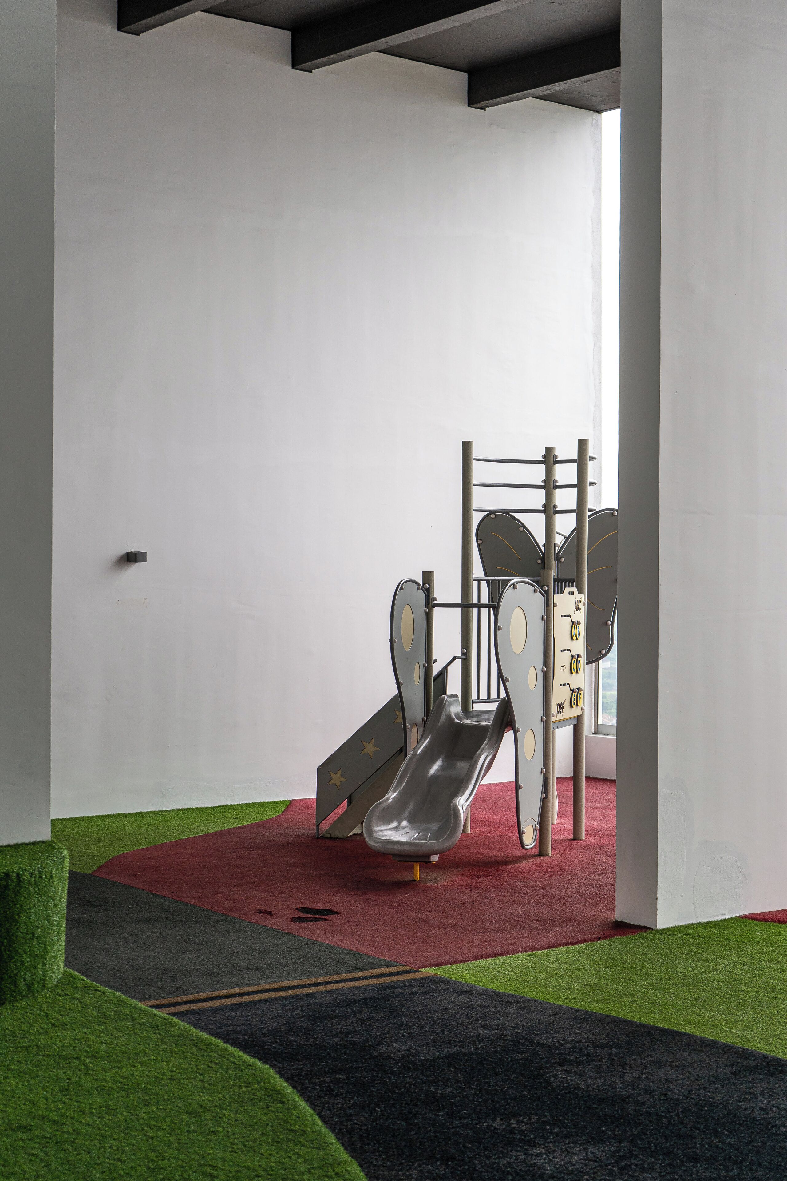 Uma área de recreação com escorrega e estrutura de escalada, piso coberto por carpete e uma janela ao fundo.