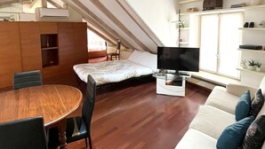 Um espaço de estar estilo loft com uma mesa de jantar de madeira, um sofá e uma televisão.