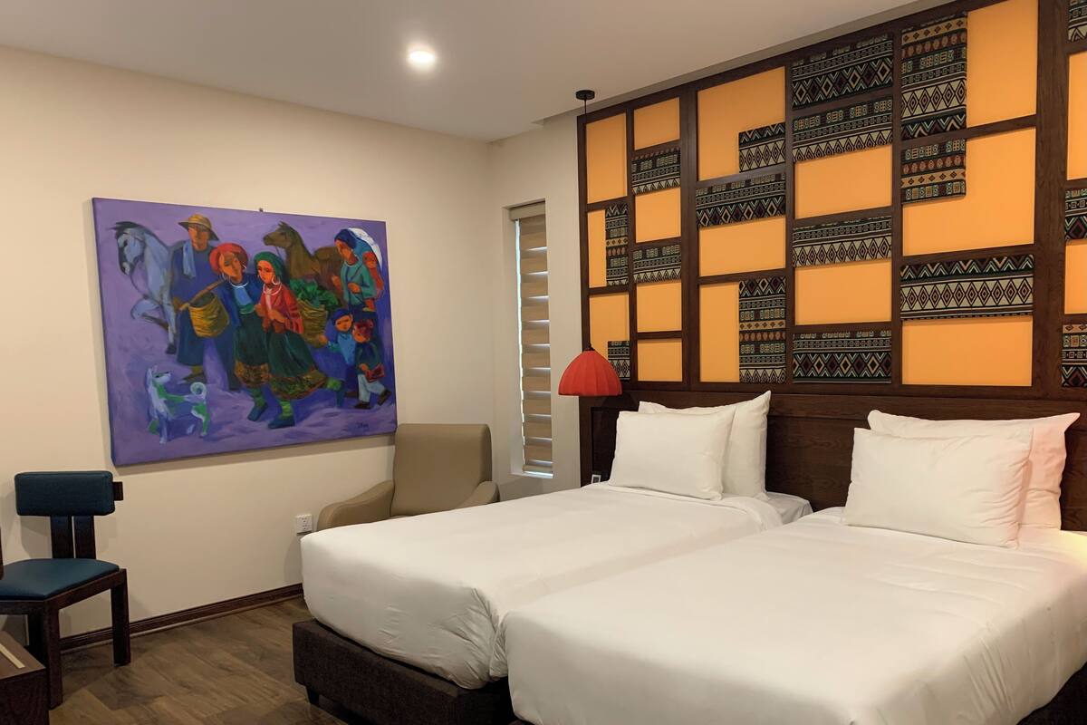 Quarto de hotel com duas camas, um quadro na parede e uma cabeceira decorativa.