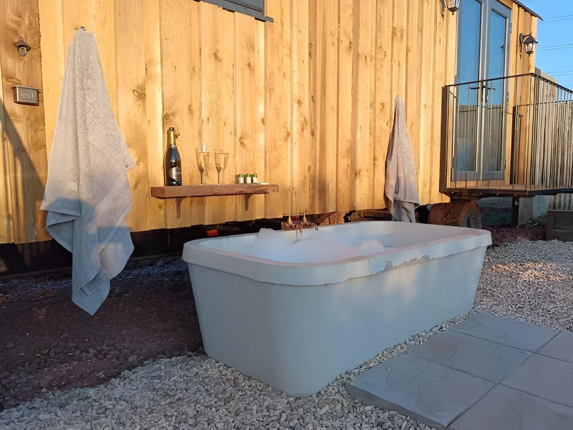 Uma cabana de madeira com banheira de hidromassagem, uma estante com garrafas e copos, e uma toalha pendurada na parede.
