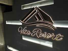 Placa do Vita Resort com design estilizado de montanha e onda, e o nome do resort em letras iluminadas.