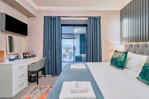 Quarto de hotel com cama, escrivaninha, televisão, vista através de uma porta de vidro e uma janela.