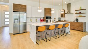 Uma cozinha moderna com uma ilha central, banquetas, eletrodomésticos de aço inoxidável e iluminação pendente.