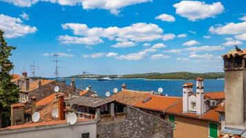 Uma cidade costeira com arquitetura tradicional, antenas parabólicas nos telhados e vista para o mar e barcos ao longe.