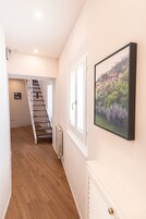 Um corredor com piso de madeira, escada, radiador e um quadro na parede.