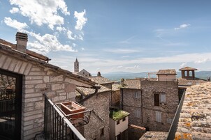 Vista de edifícios de pedra tradicionais com telhados de terracota, uma torre de sino e céu claro.