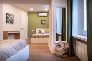 Quarto com cama, janela com cortinas, radiador e ar condicionado fixado na parede.