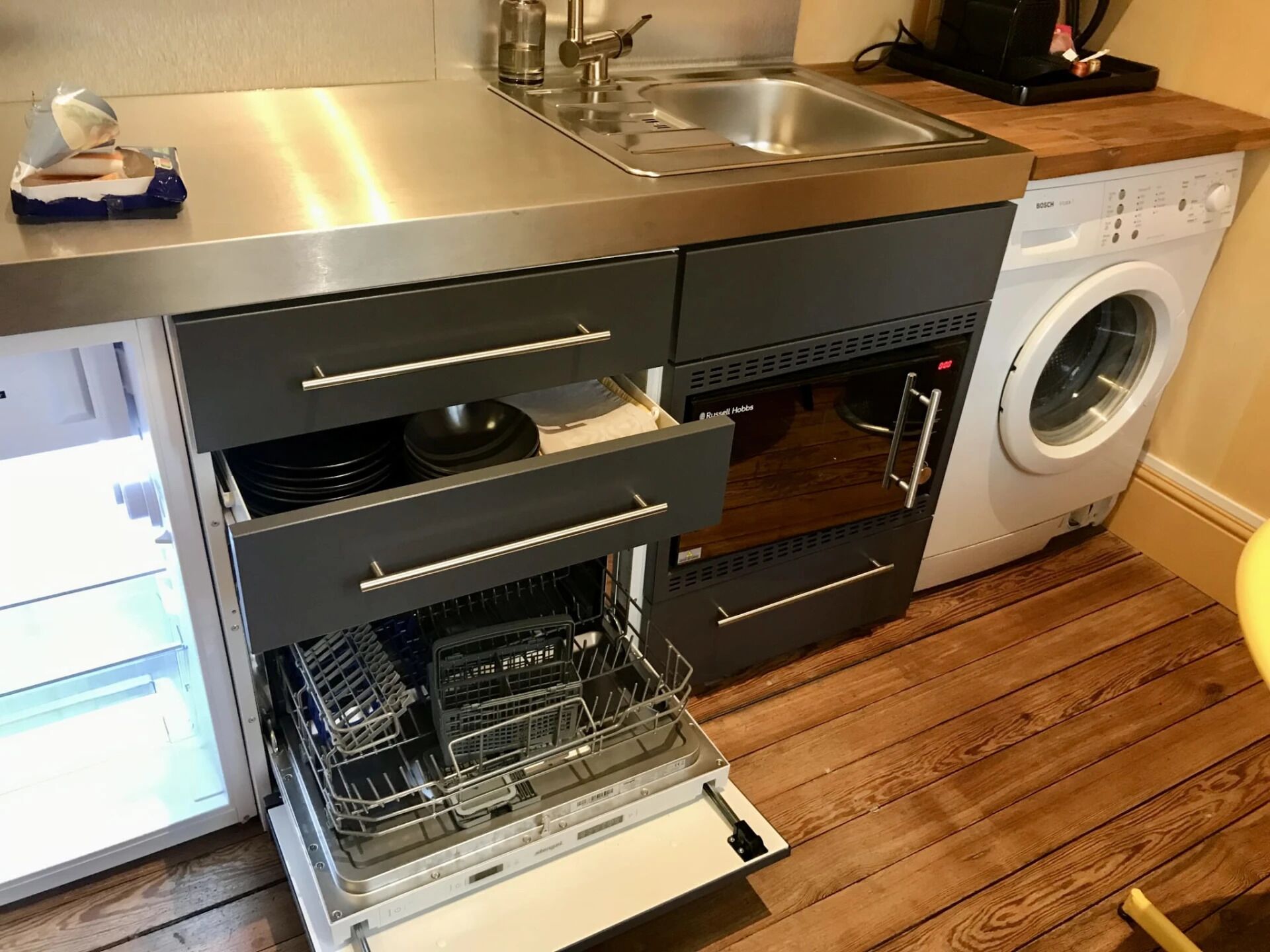 Uma cozinha compacta com lava-louças embutida, máquina de lavar e pia.
