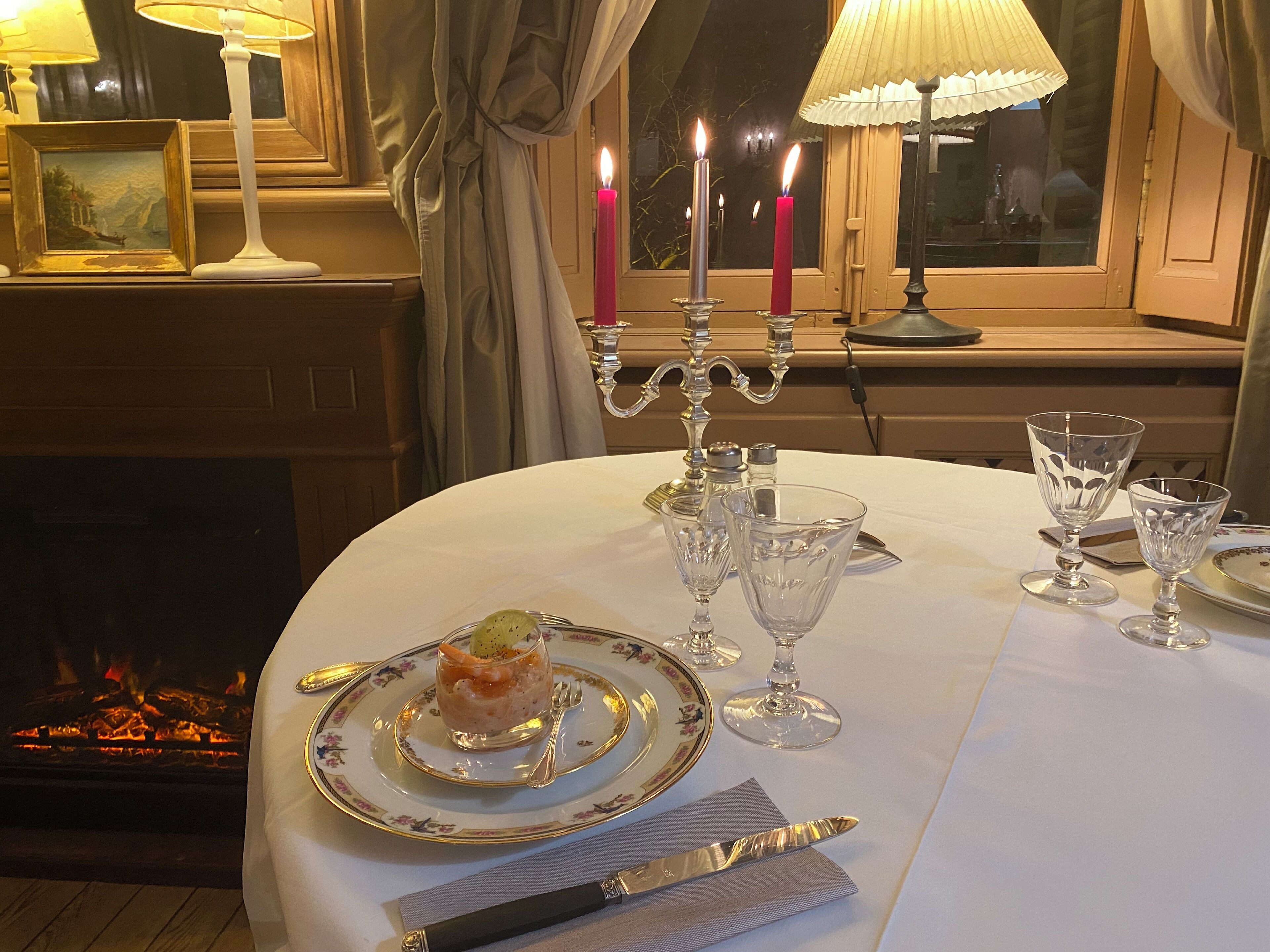 Uma mesa de jantar posta com sobremesa, copos de vinho e um candelabro com velas.