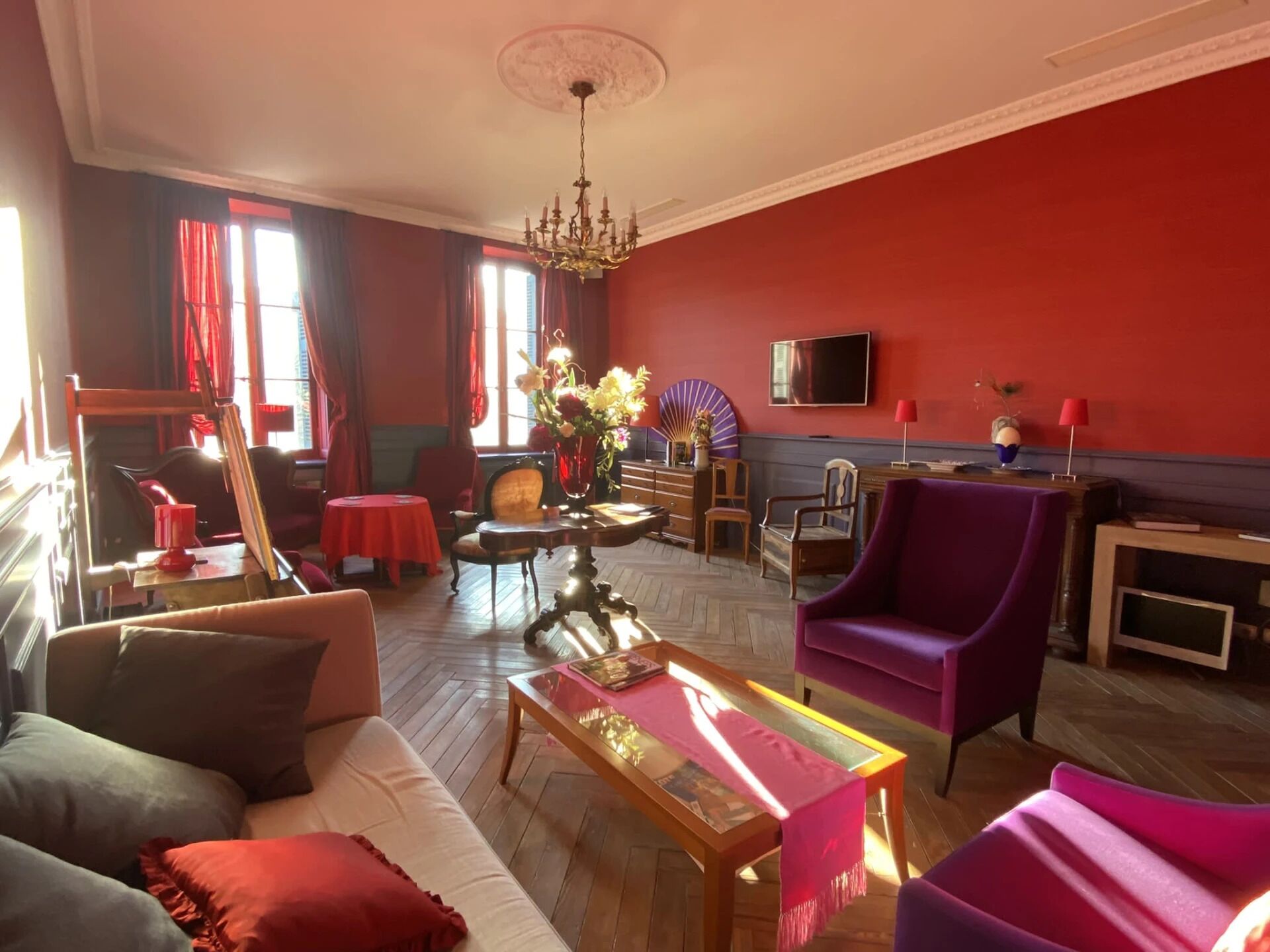 Quarto com sofá, mesa de centro, poltrona roxa, mesa de madeira com um vaso de flores e um candelabro.