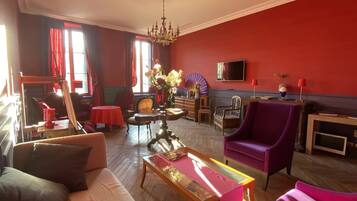 Quarto com sofá, mesa de centro, poltrona roxa, mesa de madeira com um vaso de flores e um candelabro.