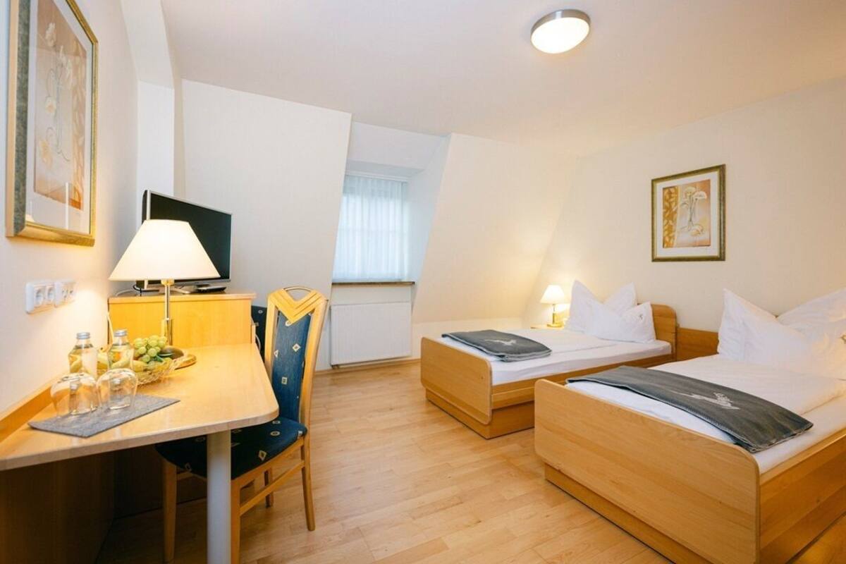 Quarto de hotel com duas camas, uma escrivaninha, uma cadeira e uma televisão.