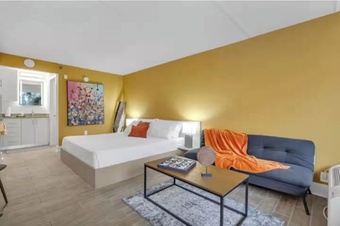Quarto moderno com cama, sofá, mesa de centro e um quadro na parede.