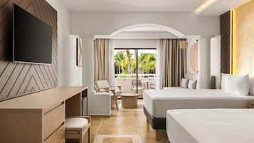 Quarto de hotel com televisão, duas camas, escrivaninha, uma cadeira e varanda com vista para palmeiras.
