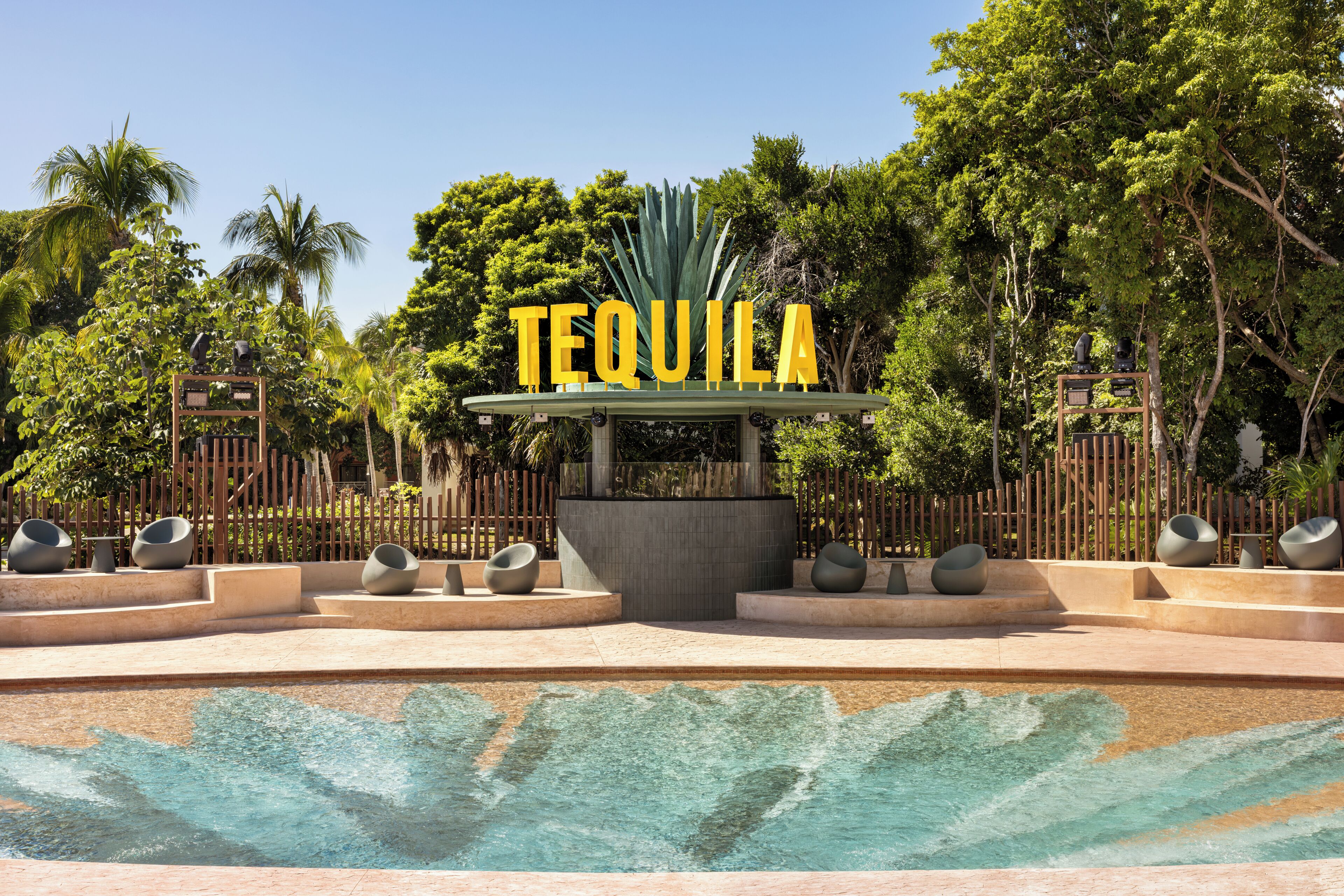 Uma área de piscina com uma placa que diz 'TEQUILA', rodeada por palmeiras e assentos modernos.