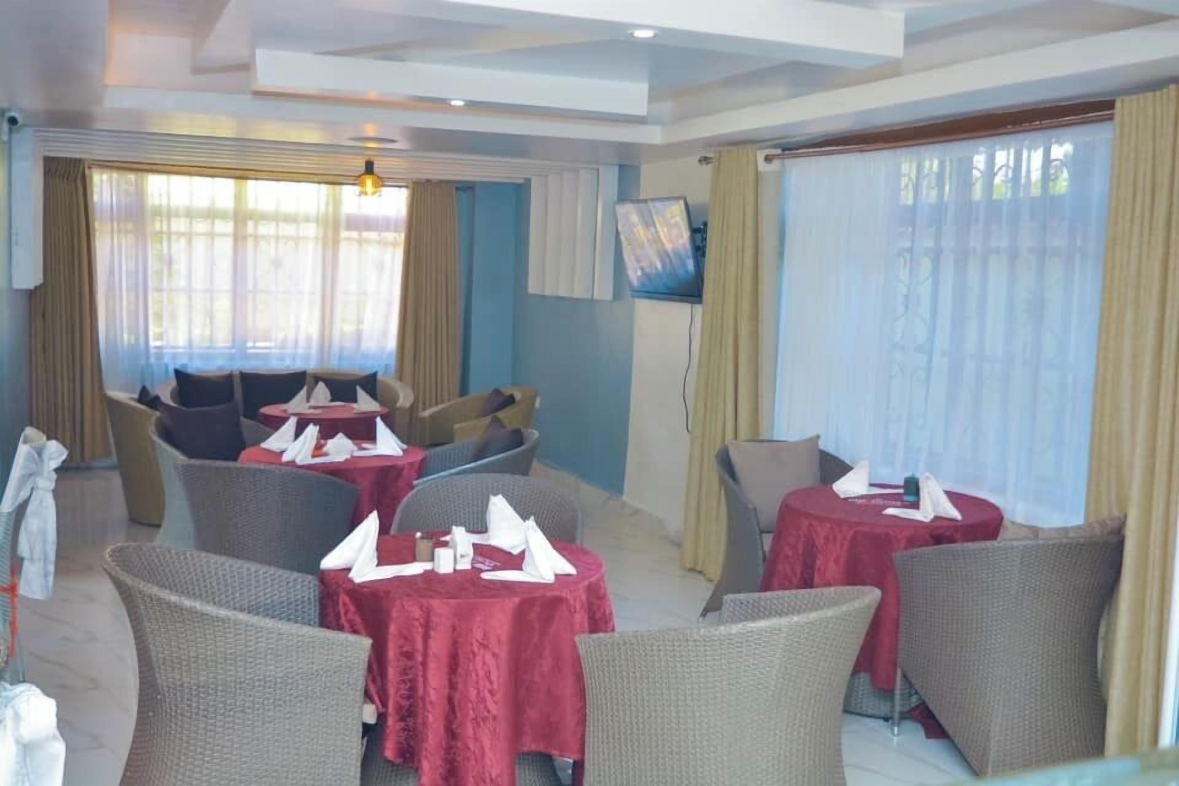 Uma área de refeições de hotel com mesas redondas cobertas por toalhas vermelhas, cadeiras de vime e um ventilador de teto.