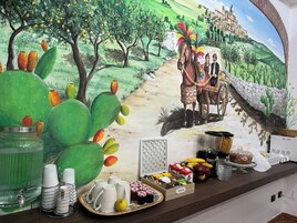 Disposição de buffet com mural, incluindo um cacto, bandeja com alimentos e dispensador de bebidas.