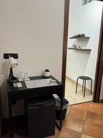 Um espaço de trabalho pequeno com escrivaninha, luminária, impressora e lixeira.