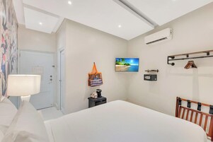 Quarto com cama, mesa de cabeceira, abajur, televisão e ar condicionado fixado na parede.