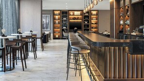 Uma área de bar moderna com um balcão comprido, banquetas e prateleiras com garrafas.