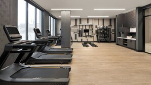 Uma academia com esteiras, aparelhos de musculação e uma janela grande.