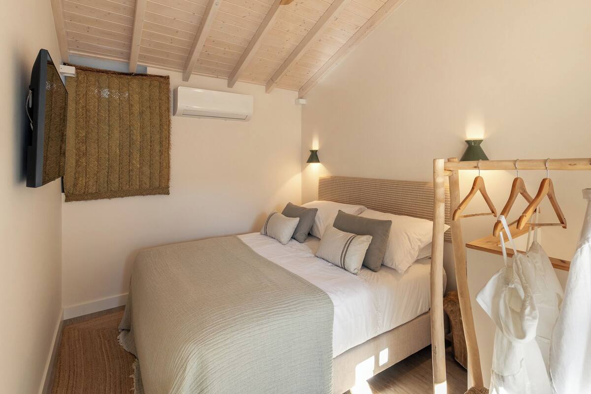 Quarto com cama, cabideiro, televisão na parede e ar condicionado.