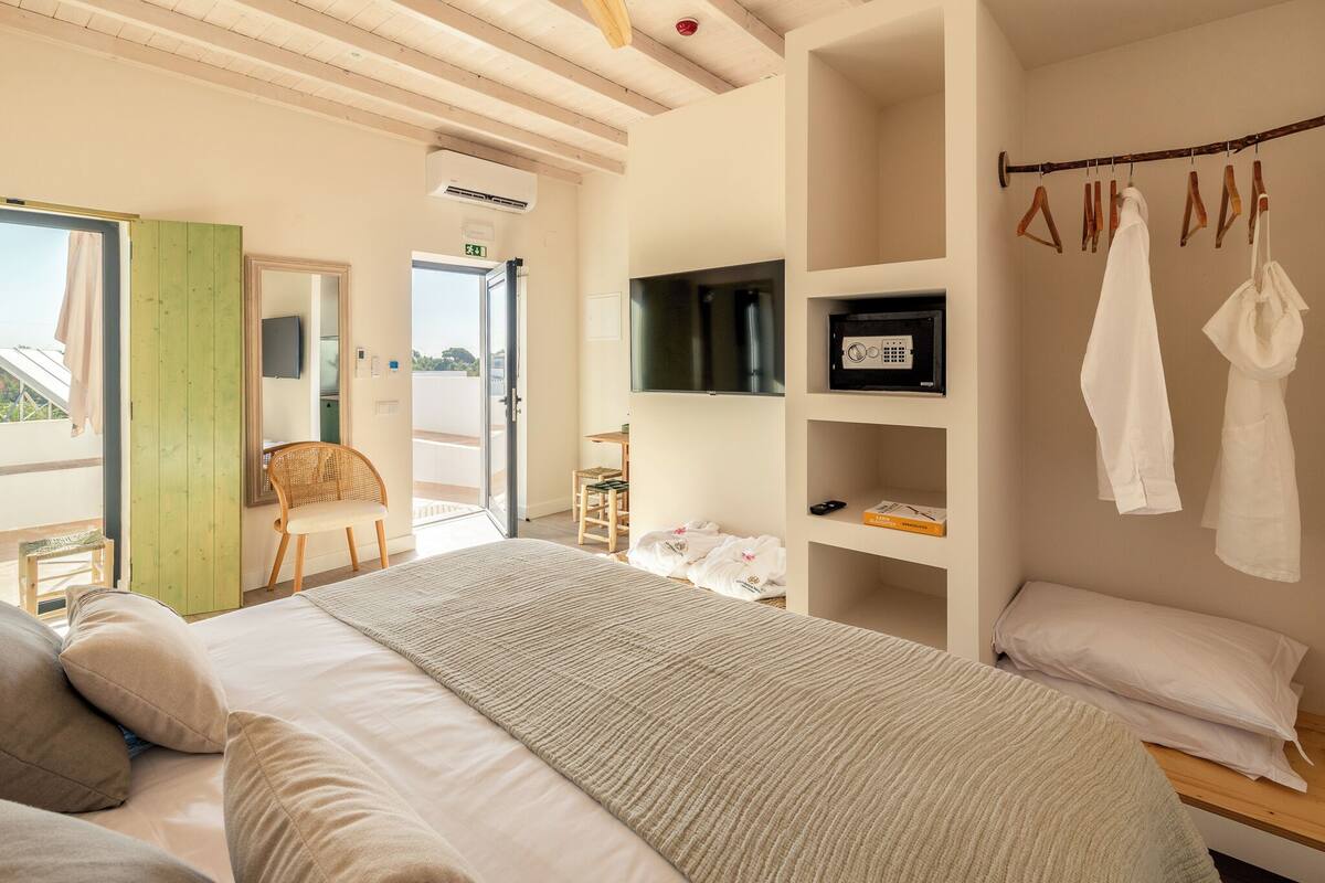 Quarto com cama, cadeira, televisão e prateleira com toalhas.
