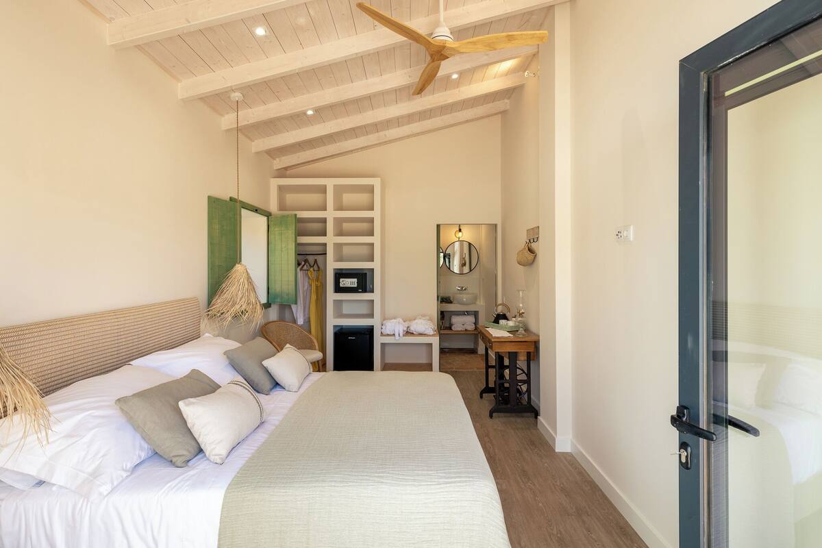 Quarto com uma cama grande, um ventilador de teto, guarda-roupa, espelho e uma pequena mesa com abajur.