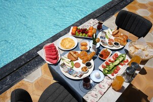 Mesa posta com diversos alimentos e bebidas à beira de uma piscina.