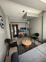 Uma sala de estar moderna com uma TV de tela plana, duas poltronas, uma mesa de centro redonda e um sofá.