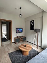 Uma sala de estar moderna com uma mesa de centro de madeira, uma TV em um móvel, um abajur e um quadro na parede.