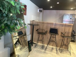 Um interior moderno com balcão de madeira, cadeiras de malha de arame preta, uma pequena mesa redonda e um vaso com planta.
