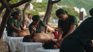Sessão de massagem com clientes deitados em macas ao ar livre, cercados por árvores e uma paisagem montanhosa.
