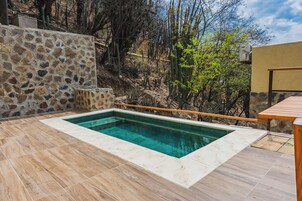 Uma piscina retangular com muro de pedra e deck de madeira.