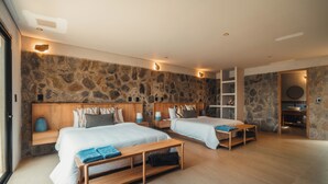 Quarto de hotel moderno com duas camas, paredes de pedra, mobiliário de madeira e prateleiras embutidas.