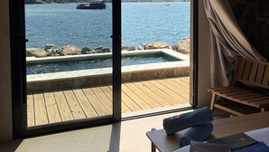 Quarto de hotel com uma grande porta de vidro deslizante que dá para uma área de piscina, uma cama, uma mesinha e uma cadeira.