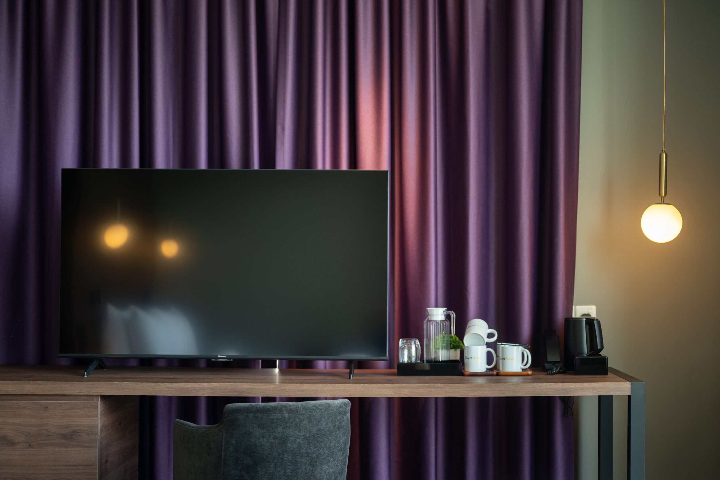 Quarto moderno com uma grande TV de tela plana sobre uma mesa de madeira, uma cafeteira e uma xícara.