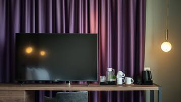 Quarto moderno com uma grande TV de tela plana sobre uma mesa de madeira, uma cafeteira e uma xícara.
