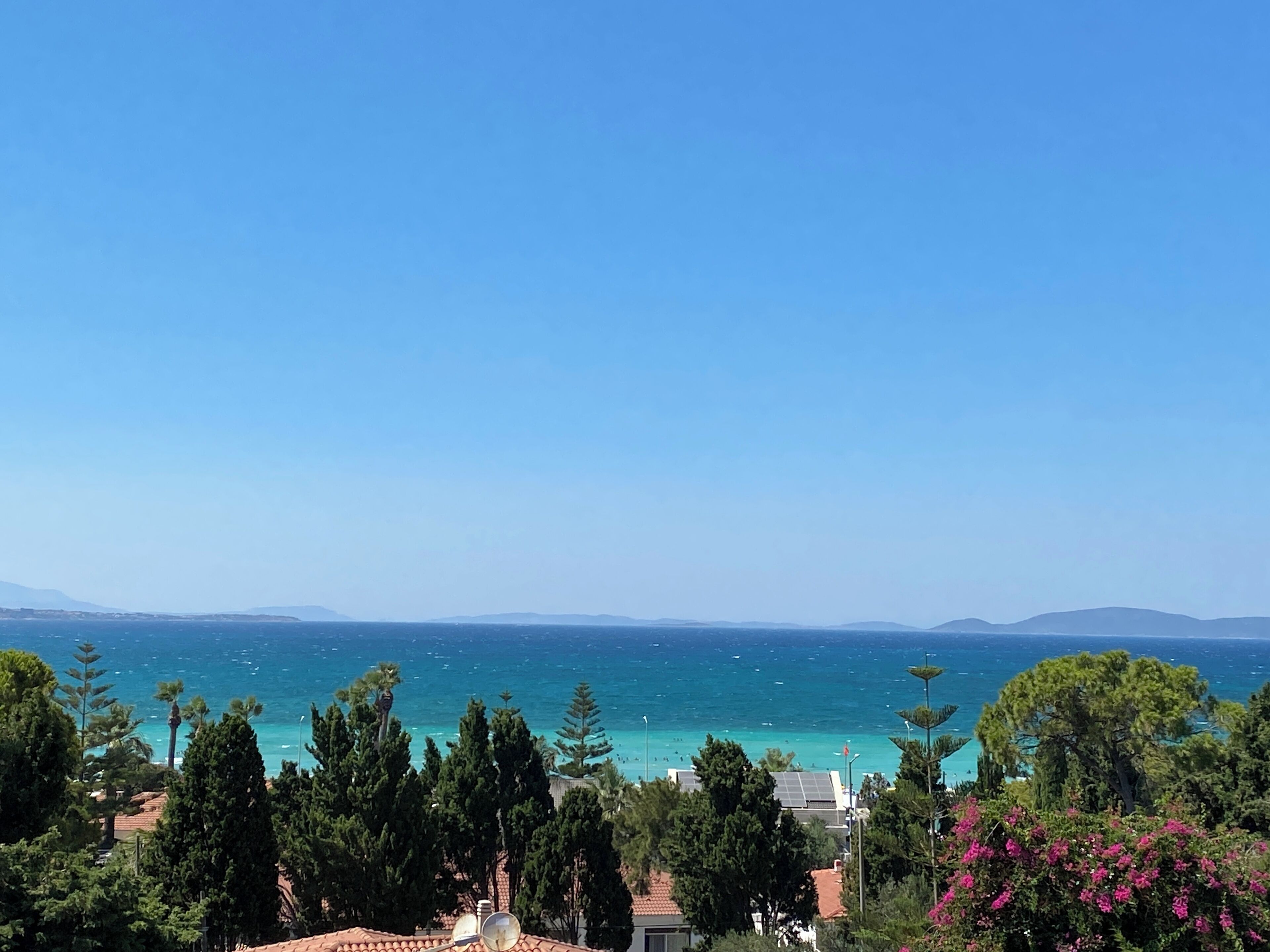 Vista costeira com céu claro, mar turquesa e uma cordilheira ao longe.