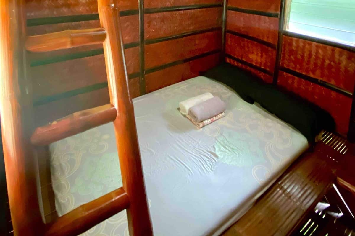 Quarto com beliche, escada, janela e uma mesinha com almofada.