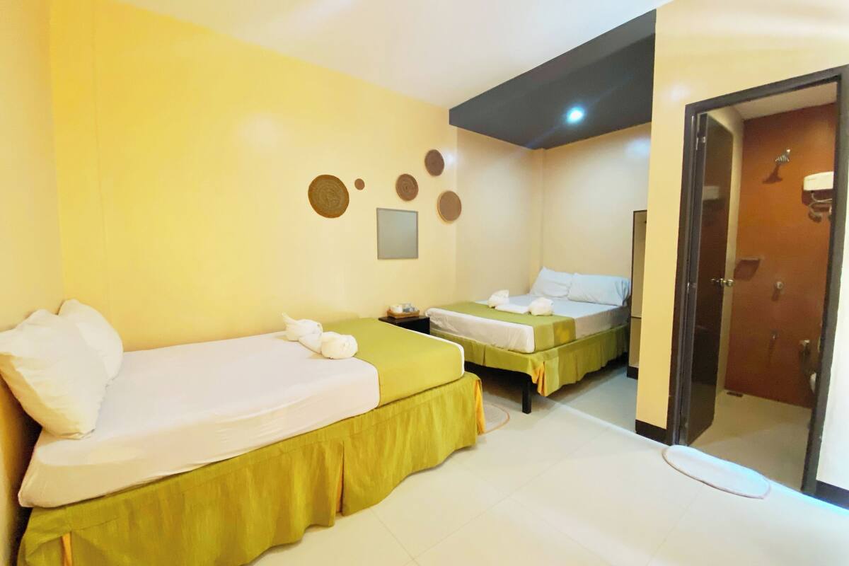 Quarto de hotel com duas camas individuais, uma pequena mesa e uma porta para o banheiro.