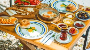 Uma mesa de madeira posta com diversos pratos, incluindo uma salada, pão e um prato com desenho de limão.