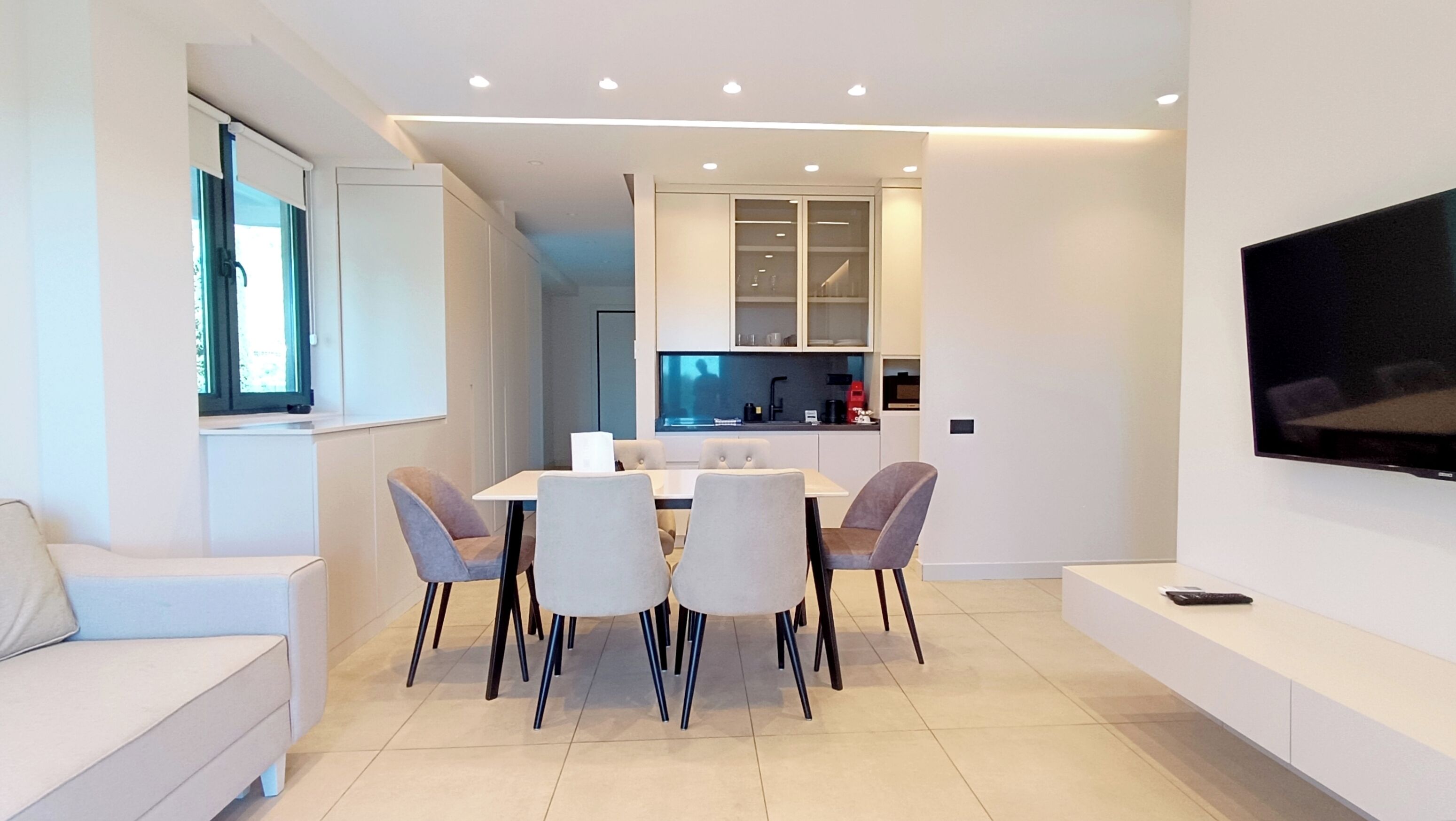 Uma sala de estar moderna com área de jantar, cozinha e televisão na parede.