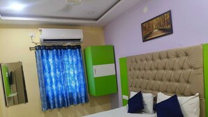 Quarto com cama, cabeceira, janela com cortinas, ar condicionado e espelho fixado na parede.