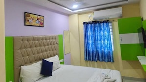 Quarto com cabeceira estofada, cama com roupa de cama branca, travesseiro azul, ventilador de teto, ar condicionado e janela com cortinas azuis.