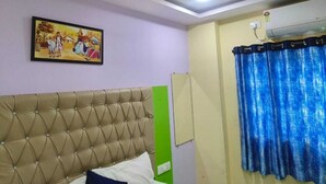 Um quarto com cabeceira estofada, cama com travesseiro branco, parede verde de destaque, cortina azul e unidade de ar condicionado fixada na parede.