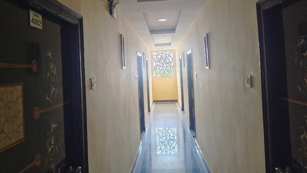 Um corredor com portas em ambos os lados, chão estampado e teto com iluminação embutida.